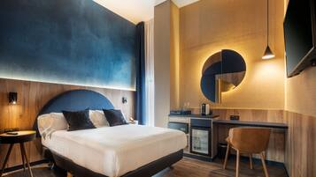 Quarto de hotel moderno com uma cama grande, uma escrivaninha, uma cadeira e uma televisão.