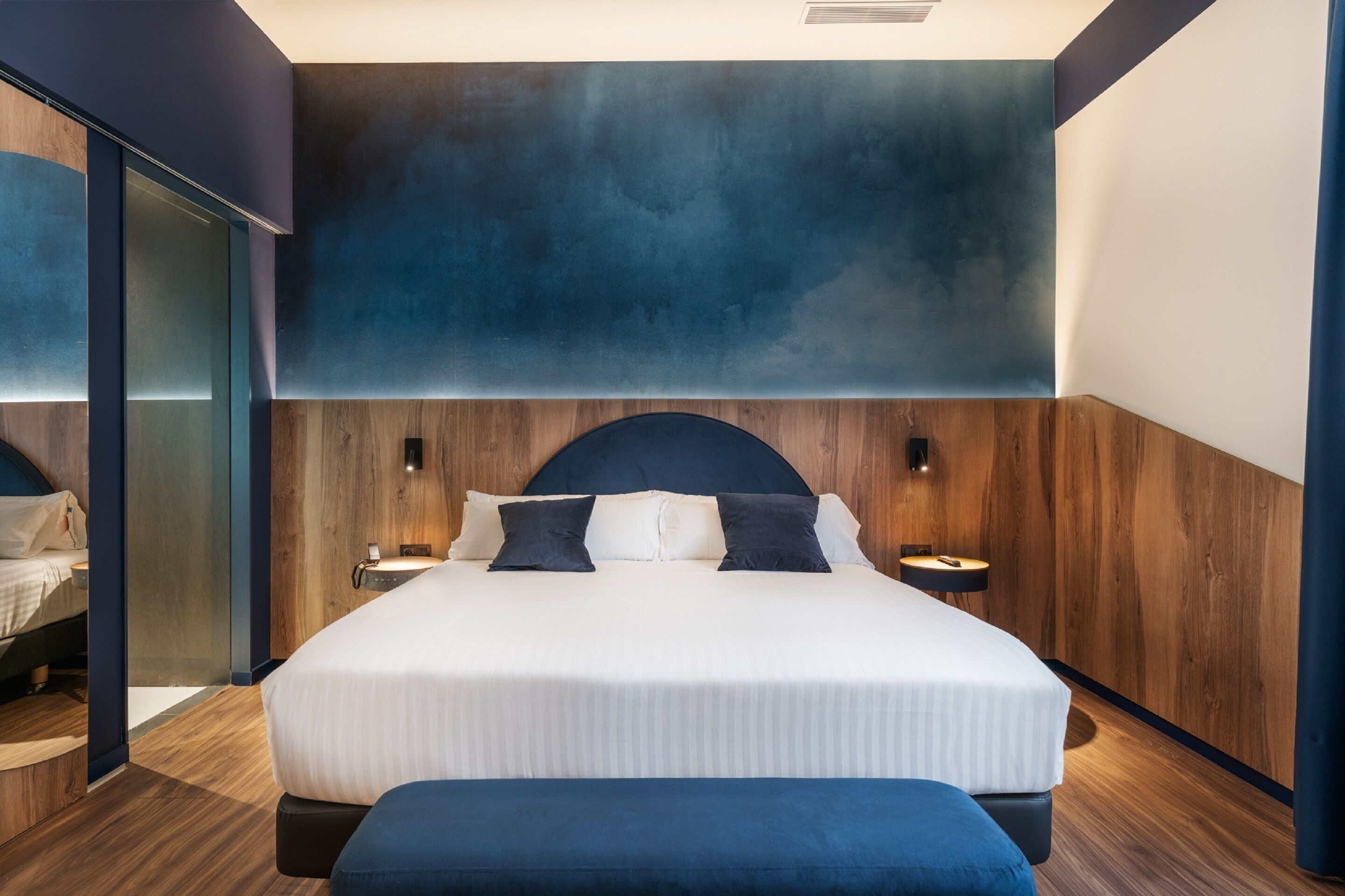Quarto de hotel moderno com uma cama grande, painéis de madeira nas paredes e teto escuro.