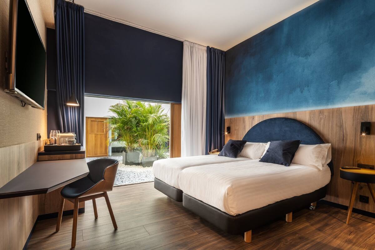Quarto de hotel moderno com uma cama grande, uma escrivaninha e vista para o verde lá fora.