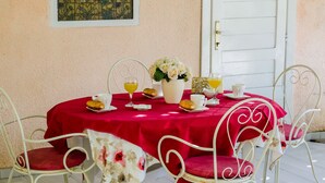 Uma mesa de jantar com toalha vermelha, cadeiras de metal branco e um vaso de flores.