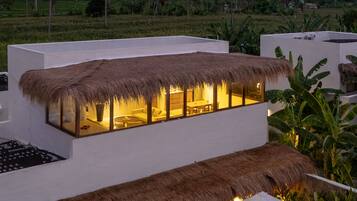 Uma villa moderna com telhado de palha, piscina e vista para colinas exuberantes.