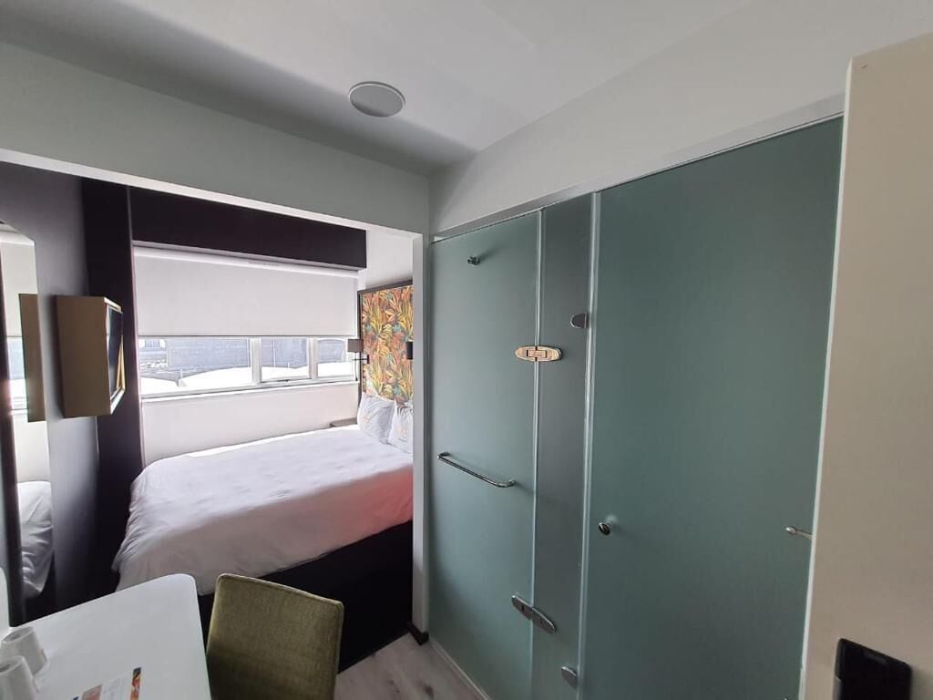 Quarto de hotel com cama, secretária, guarda-roupa e janela com vista para a cidade.
