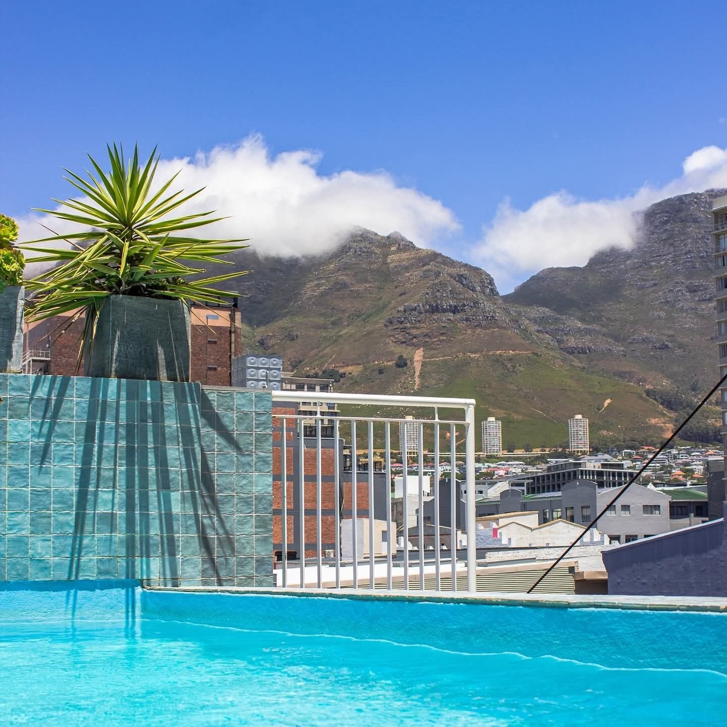 Uma piscina com montanhas ao fundo, um edifício com fachada de tijolos e um céu claro.