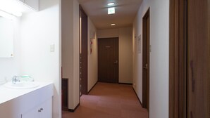 Um corredor estreito com uma pia branca e armários à esquerda, uma porta de madeira com um número no centro e outra porta de madeira à direita.