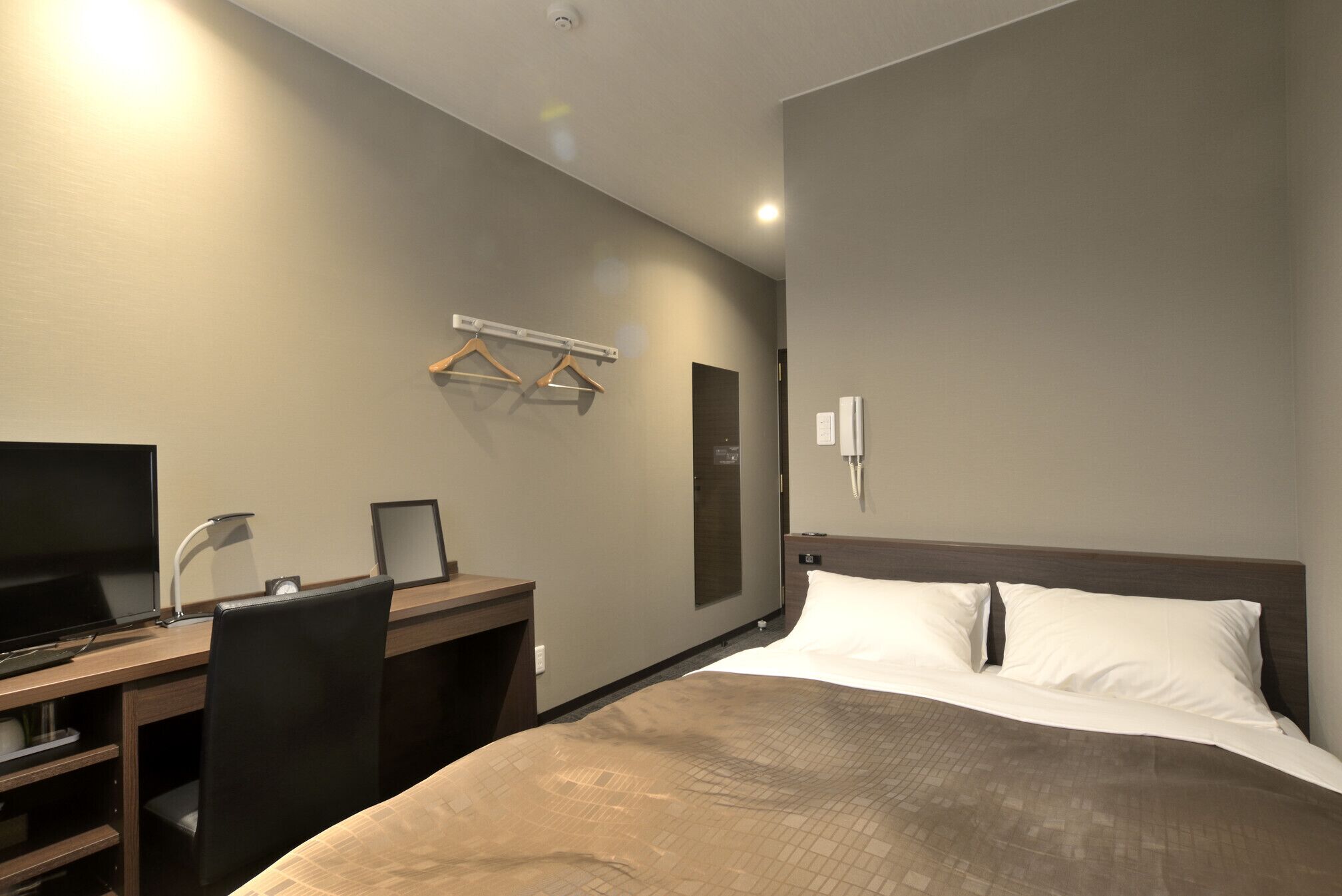 Quarto de hotel com cama, secretária com computador, cadeira, televisão e telefone fixado na parede.