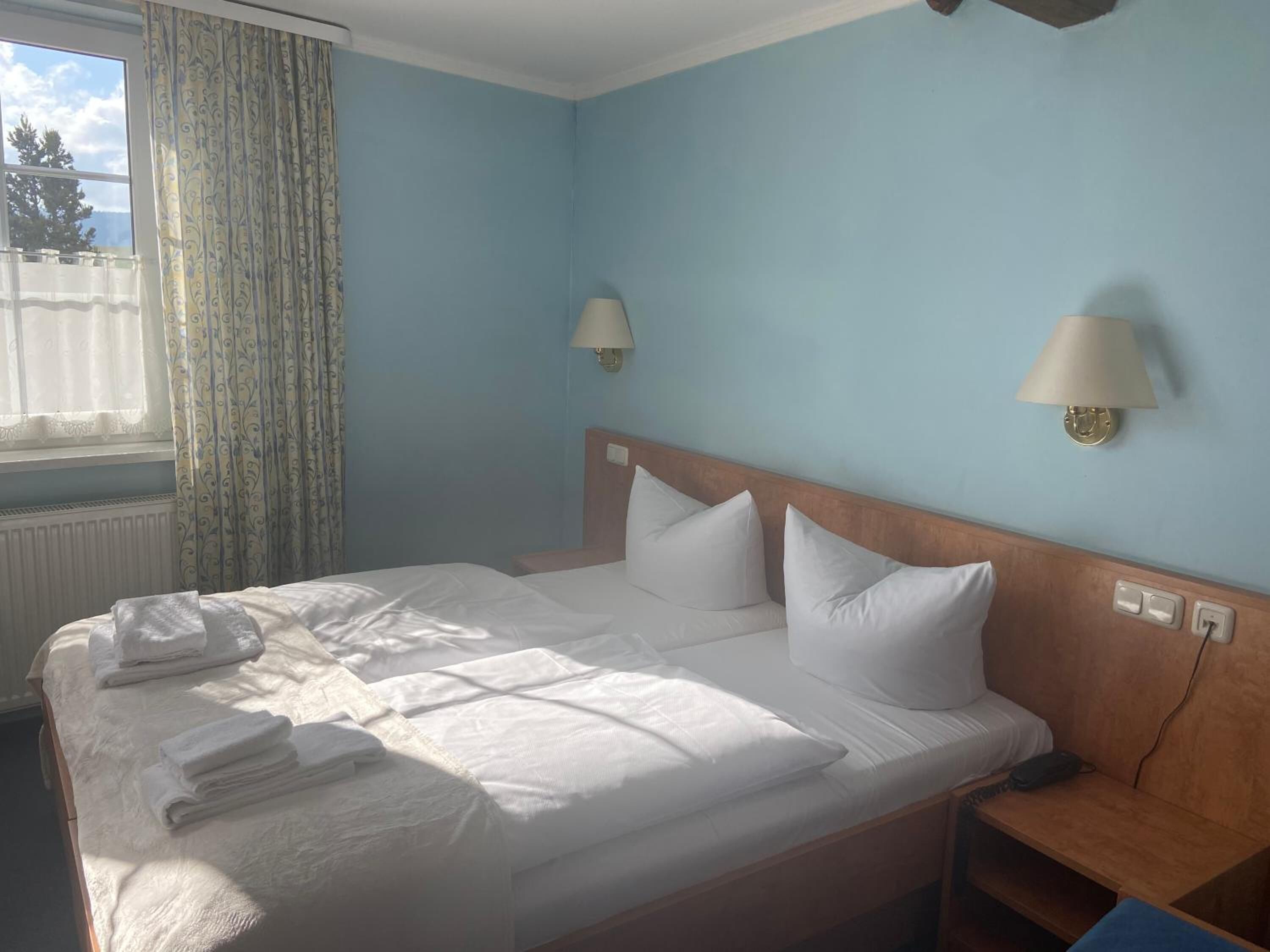 Quarto de hotel com uma cama grande, duas luminárias de cabeceira, uma cabeceira de madeira e uma janela com cortinas.
