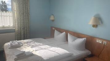 Quarto de hotel com uma cama grande, duas luminárias de cabeceira, uma cabeceira de madeira e uma janela com cortinas.