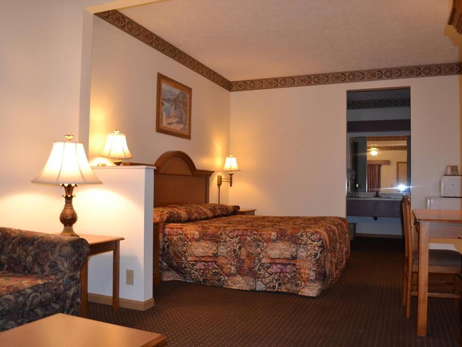 Quarto de hotel com cama, uma cadeira, escrivaninha e duas luminárias.