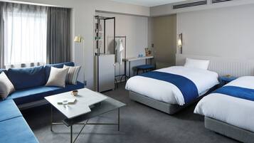 Quarto de hotel com sofá, duas camas, escrivaninha e espelho.