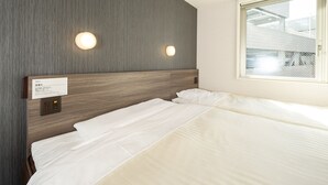 Quarto de hotel com duas camas, cabeceira de madeira, luminária na parede e janela com persianas.