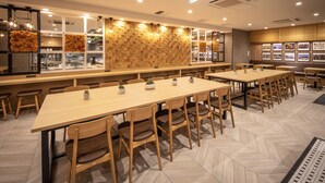 Restaurante com várias mesas e cadeiras de madeira, um padrão de piso em herringbone e uma parede decorada com quadros.