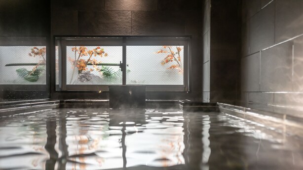 Uma grande piscina interior com paredes de vidro transparente, permitindo vistas da vegetação exterior.