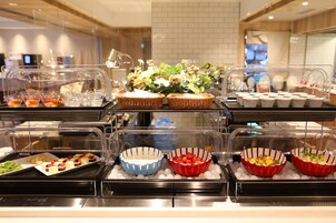 Buffet com diversos alimentos, incluindo frutas, sobremesas e um arranjo floral.