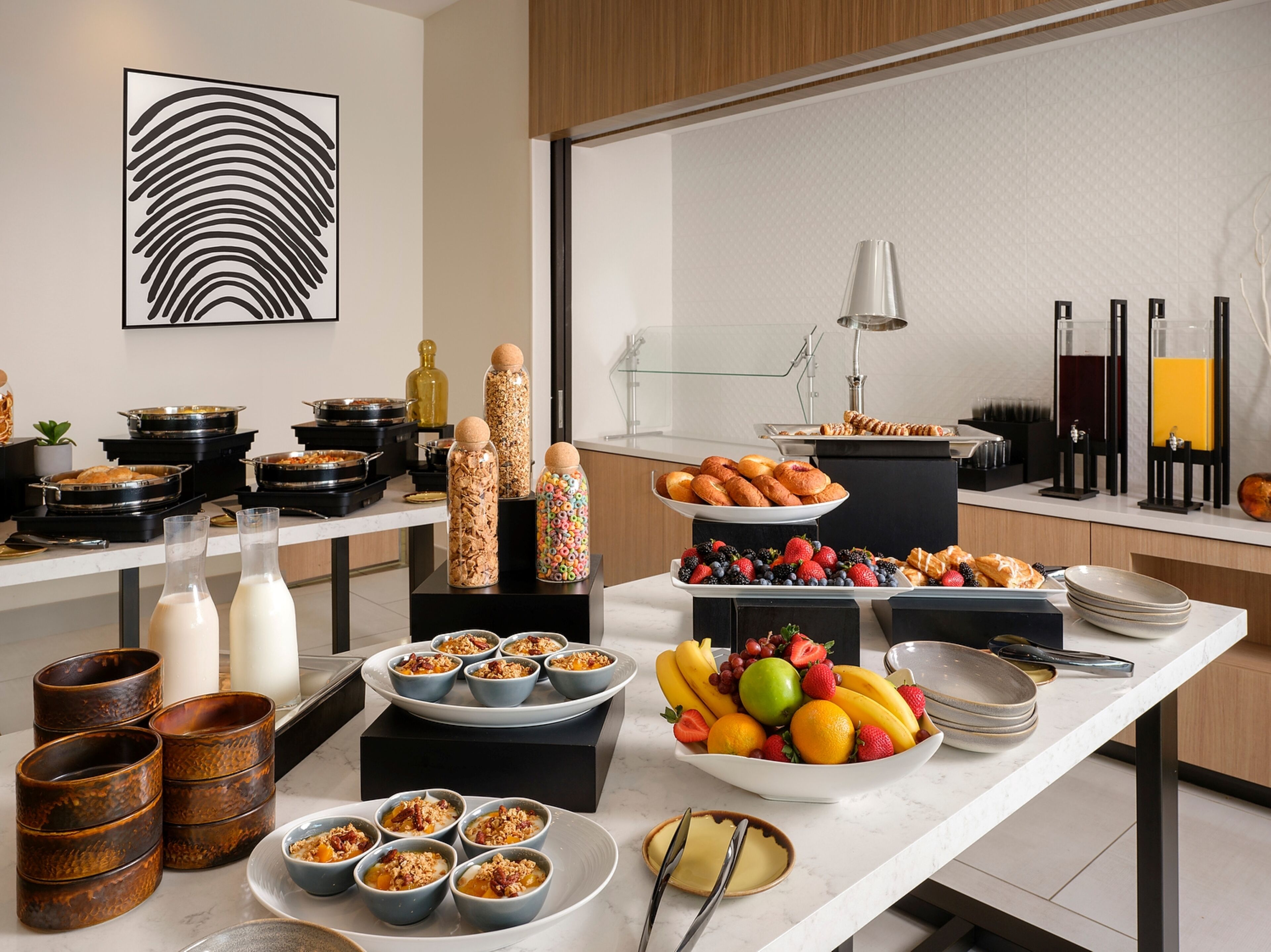 Disposição de buffet com diversos alimentos, incluindo frutas, doces e bebidas, organizados sobre uma mesa.