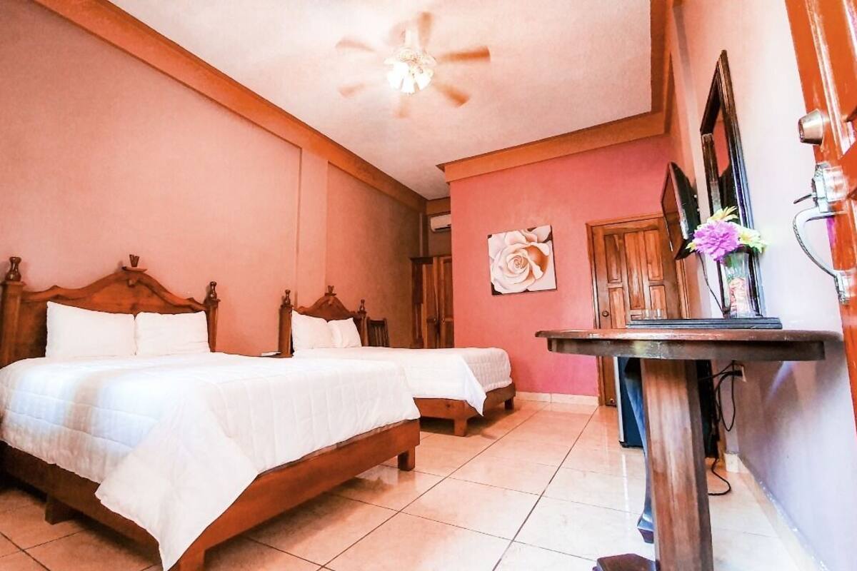 Quarto com duas camas de madeira, uma mesinha e um ventilador de teto.