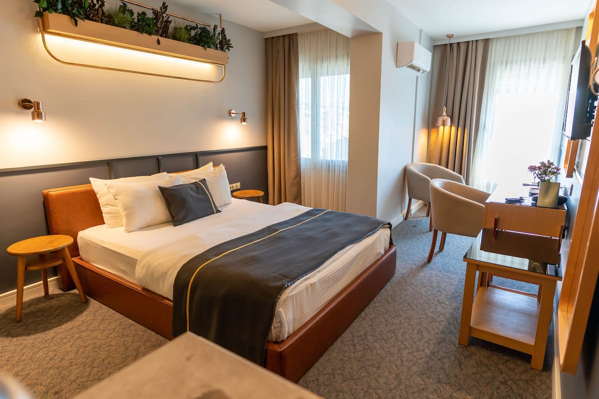 Quarto de hotel com uma cama grande, uma escrivaninha, uma cadeira e uma mesinha.