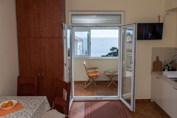 Cozinha com vista para o mar, mesa de jantar com uma tigela de frutas e uma TV fixada na parede.