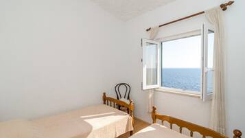 Quarto com duas camas, janela com cortinas e vista para o mar.