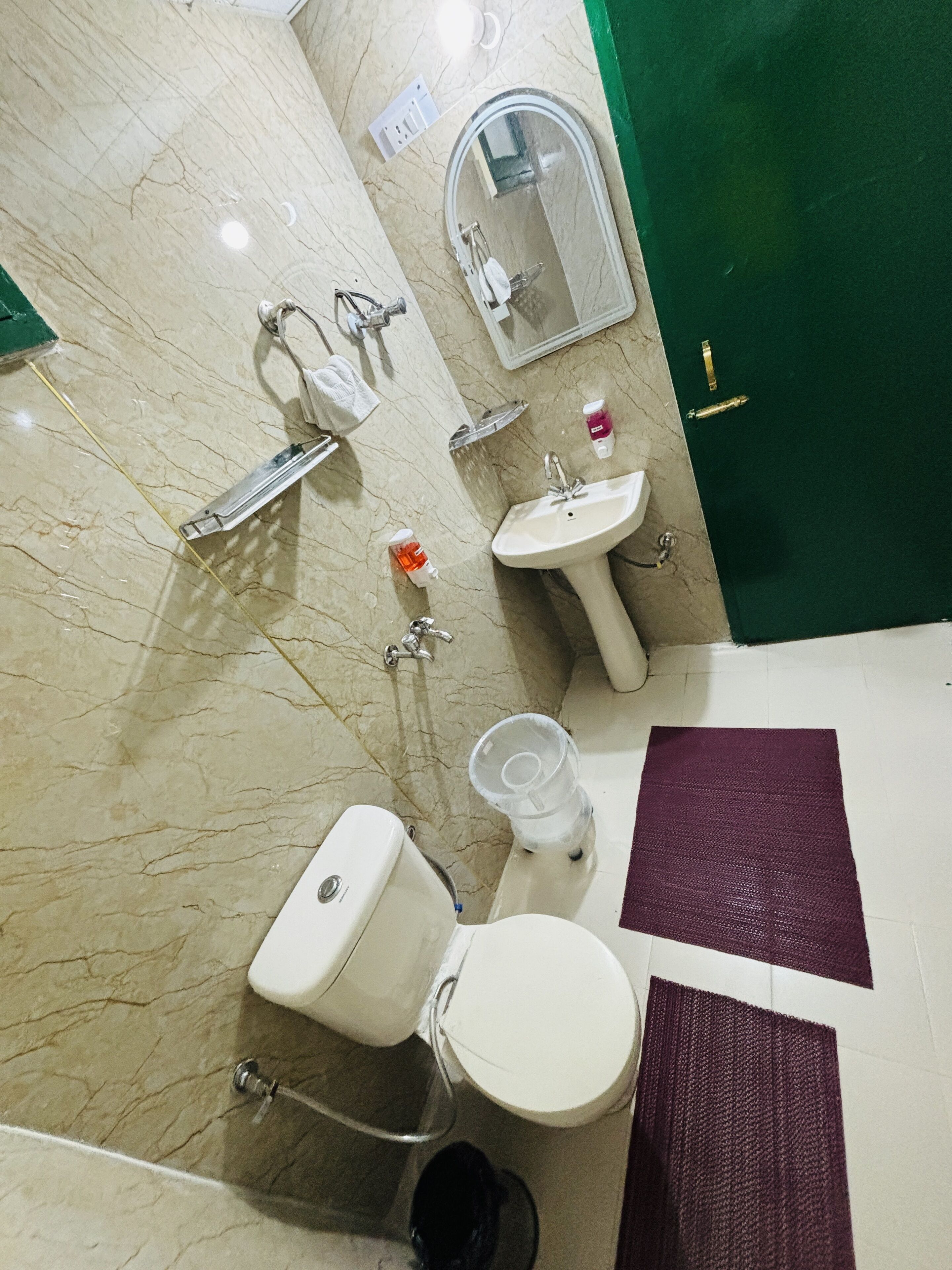 Casa de banho com sanita, lavatório e chuveiro. Há um espelho sobre o lavatório e uma porta verde ao fundo.