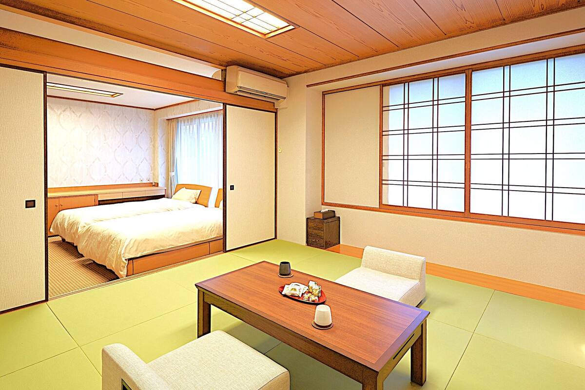 Um quarto tradicional japonês com tatame, uma mesa de madeira baixa, um sofá e uma cama com futon.