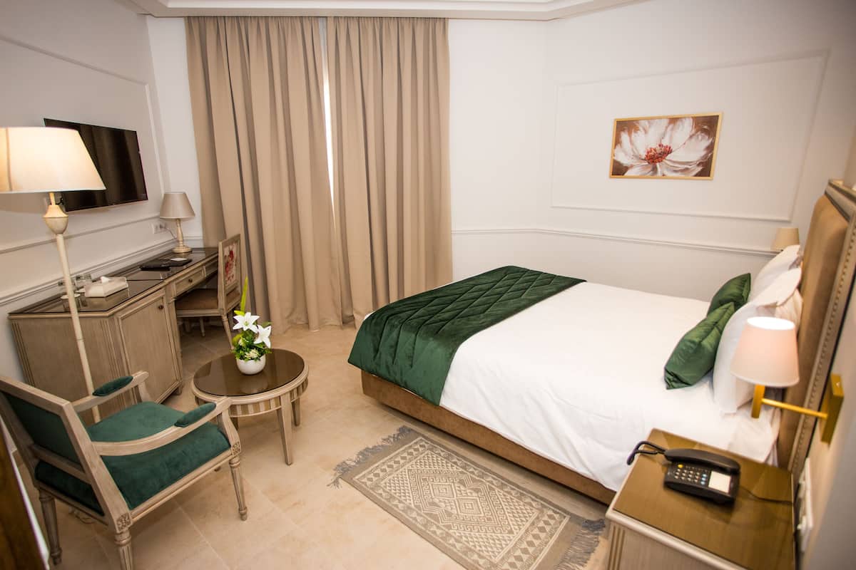 Quarto de hotel com uma cama, escrivaninha, cadeira, televisão, telefone e um quadro na parede.