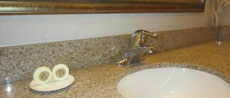 Casa de banho com bancada de granito, lavatório branco e espelho sobre o lavatório.