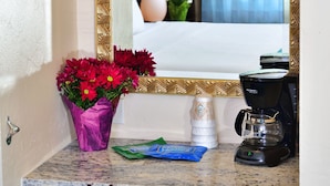 Casa de banho de hotel com espelho, um vaso de flores, máquina de café e dispensador de toalhas.