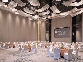 Sala de conferências com mesas redondas, cadeiras brancas e um ecrã grande exibindo a marca do hotel.