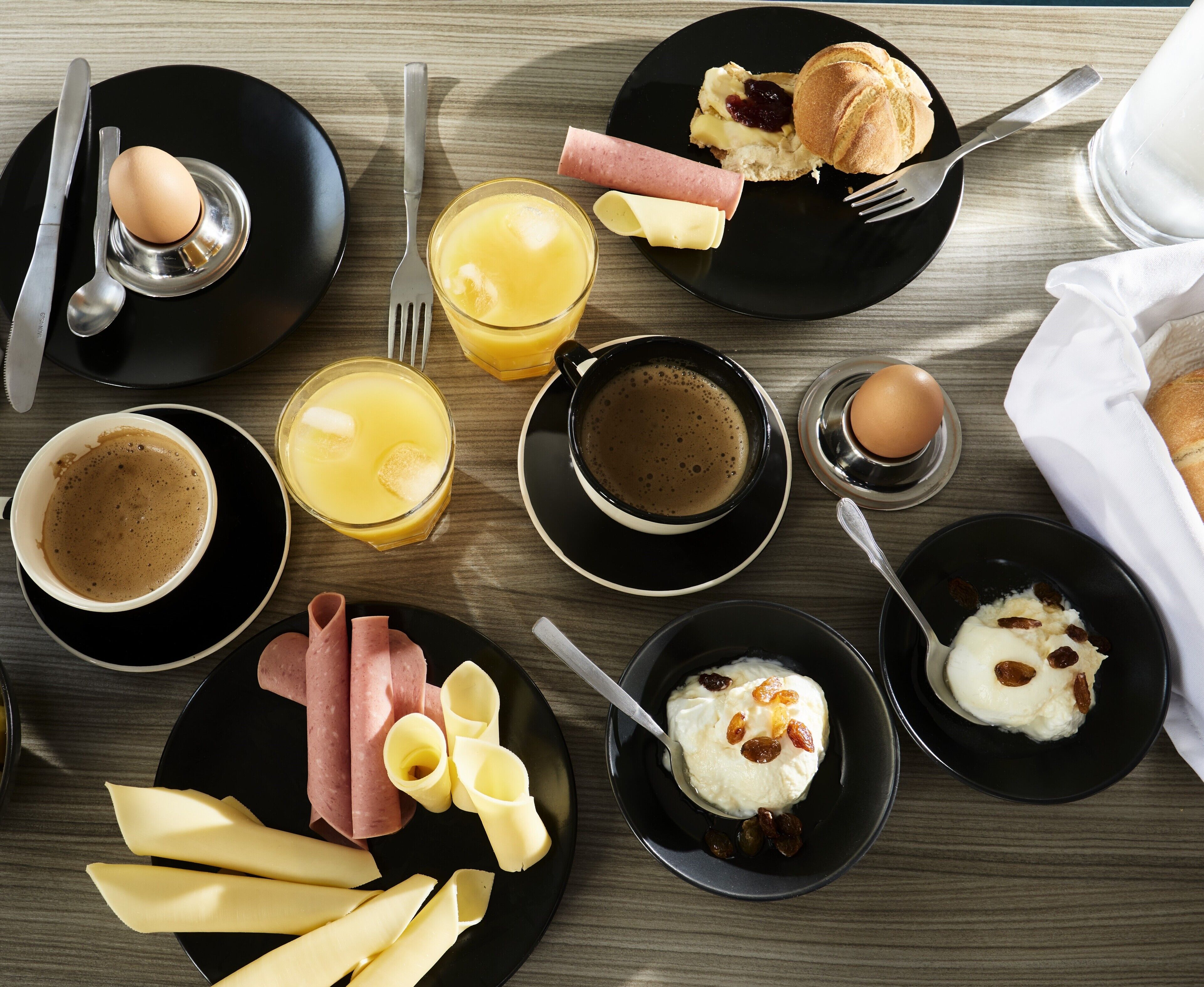 Disposição de café da manhã com pratos de ovos, presunto e doces, acompanhados de xícaras de café e suco de laranja.
