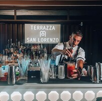 Um bartender em um bar com uma placa indicando "TERRAZZA SAN LORENZO".