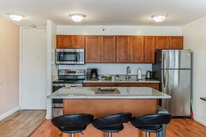 Cozinha moderna com armários de madeira, eletrodomésticos de aço inoxidável e uma ilha central com banquetas.