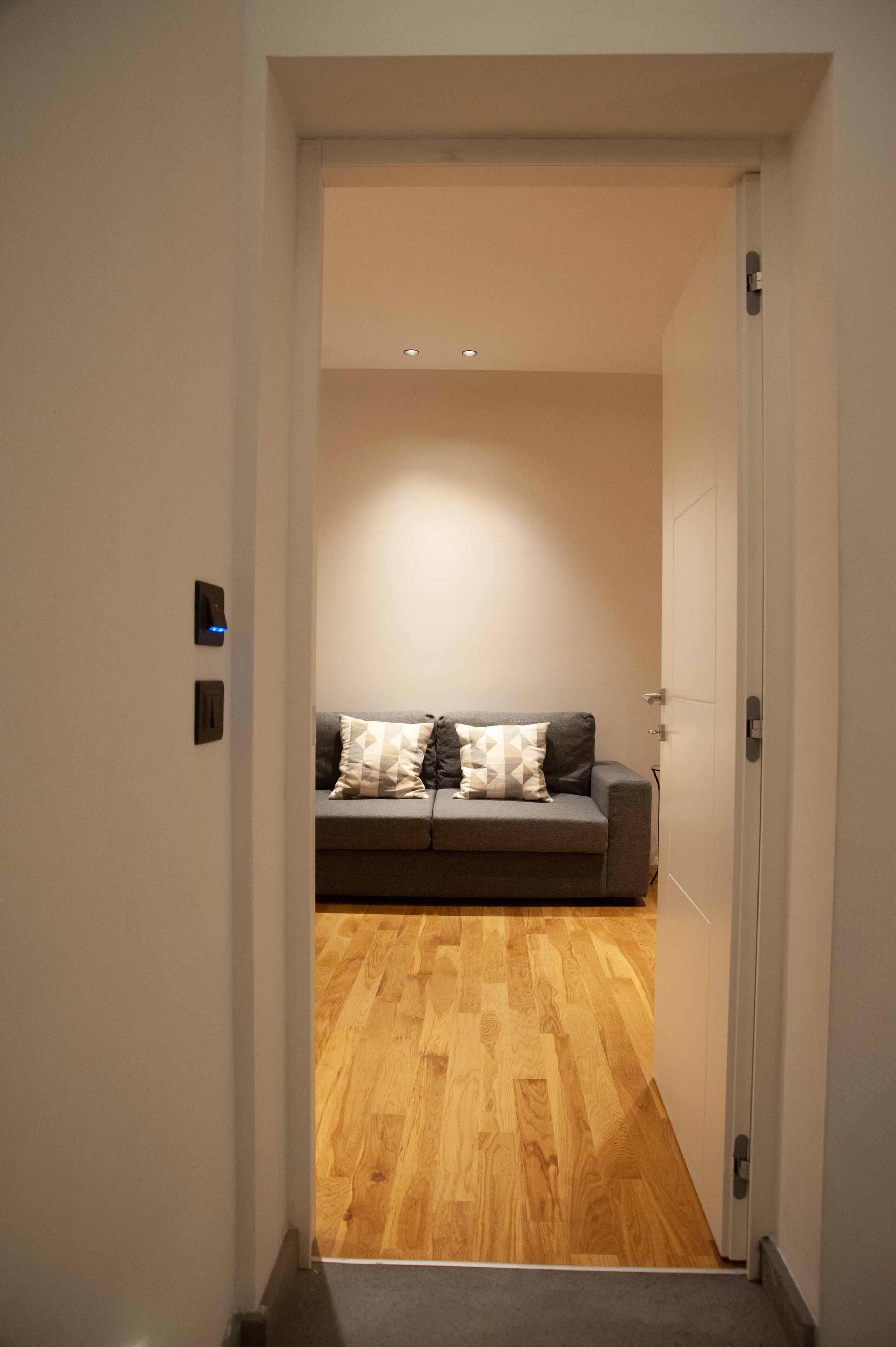 Um corredor estreito que dá para uma sala de estar com um sofá e piso de madeira.