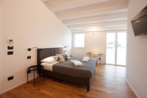 Quarto moderno com cama, mesas de cabeceira, escrivaninha e televisão.