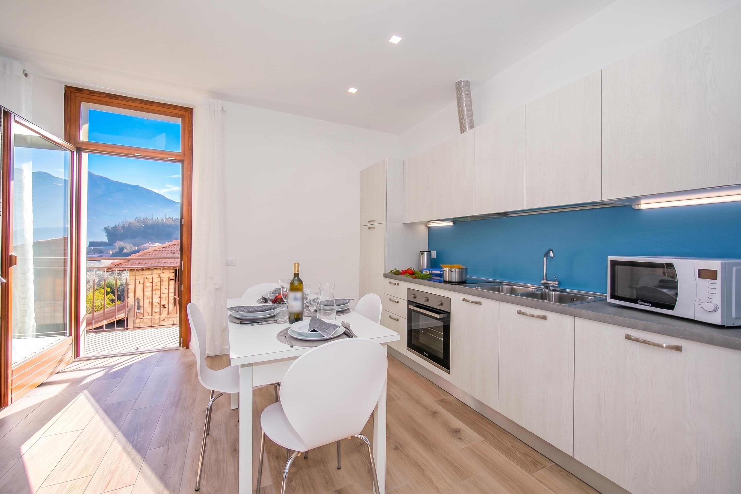 Uma cozinha moderna com armários brancos, painel azul e micro-ondas embutido.