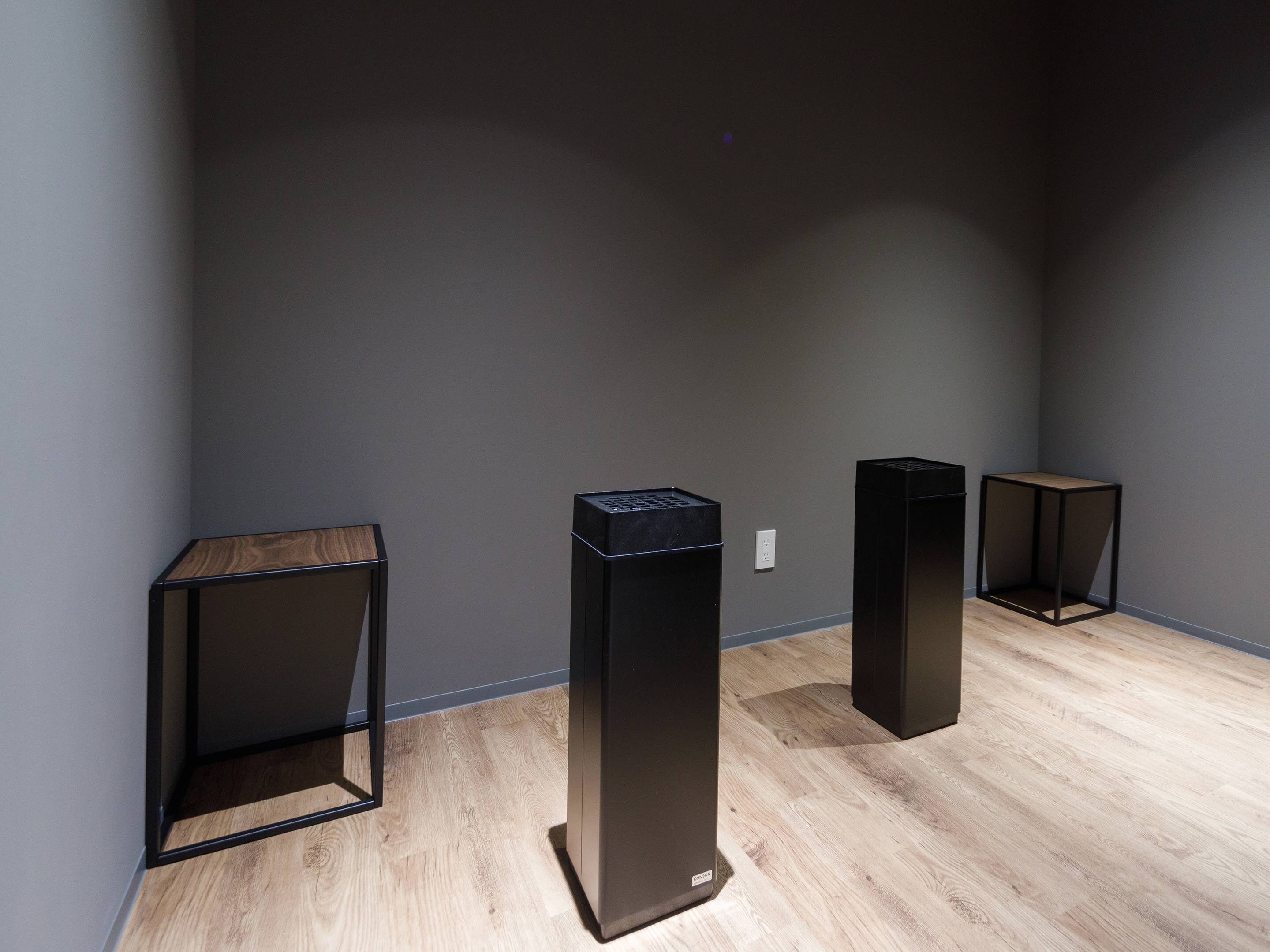 Três alto-falantes pretos numa sala com paredes cinzentas e soalho de madeira.