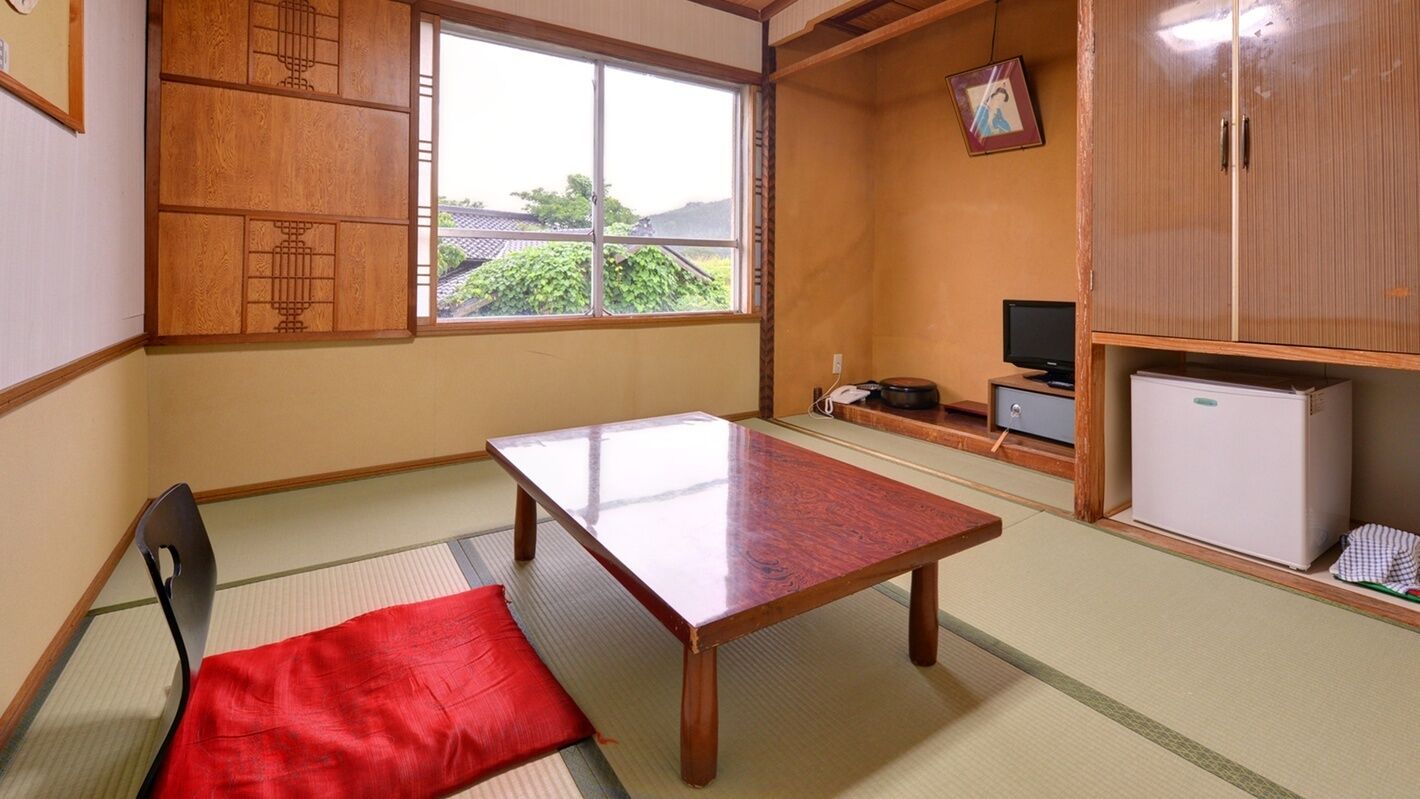 Quarto japonês tradicional com tatames, uma mesa de madeira baixa, uma televisão e um frigorífico.