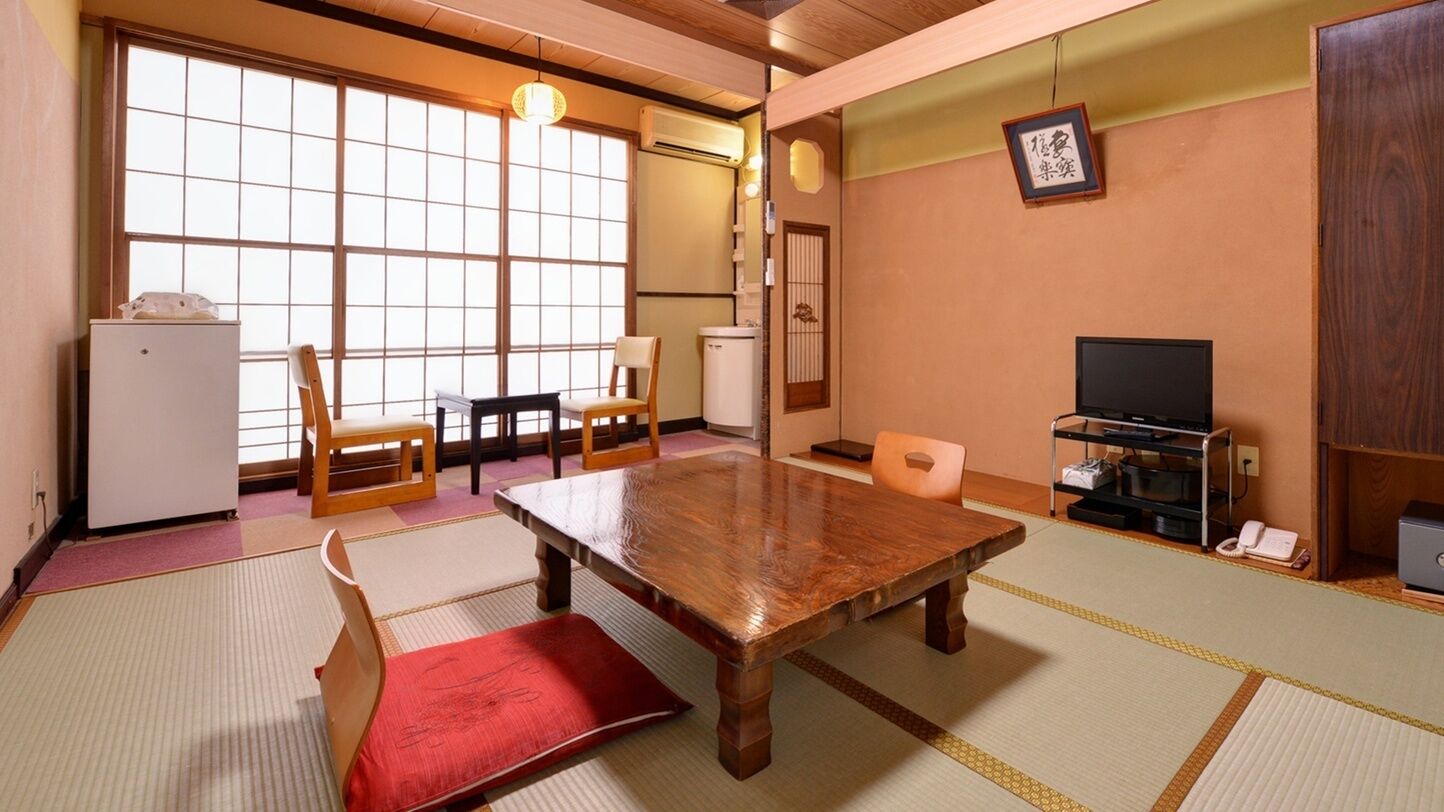 Um quarto japonês tradicional com tatames, uma mesa de madeira, uma televisão e um frigorífico.