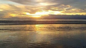 Uma praia ao pôr do sol, águas calmas refletindo o céu.