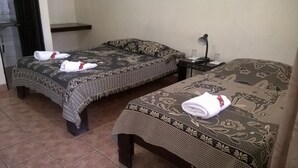 Duas camas com colchas estampadas, uma mesa de cabeceira com abajur e uma toalha em cada cama.