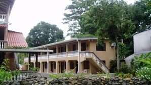 Um edifício de dois andares com varanda e parede de pedra em frente.