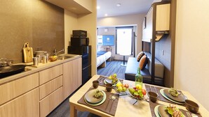 Quarto de hotel compacto com cozinha compacta, área de jantar com mesa posta, cama e pequeno espaço de estar.
