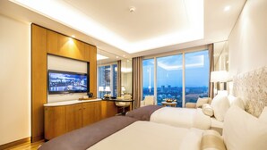 Quarto de hotel moderno com uma cama grande, uma escrivaninha, uma televisão e vista para a cidade.