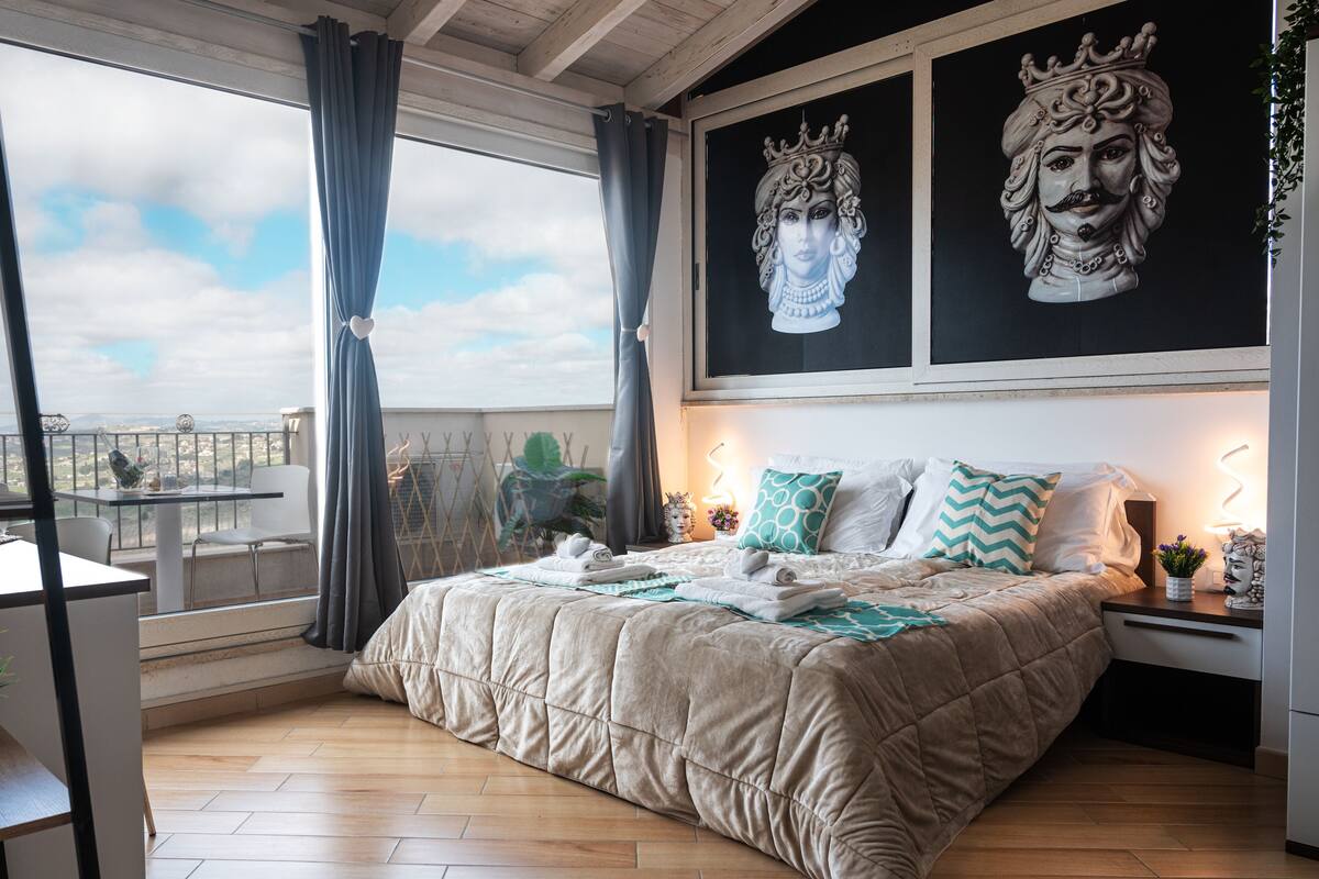 Quarto com uma cama grande, varanda com vista e duas obras de arte na parede.