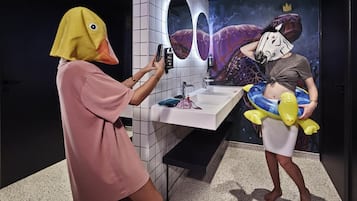 Um banheiro com pia branca, espelho e parede com um mural decorativo.