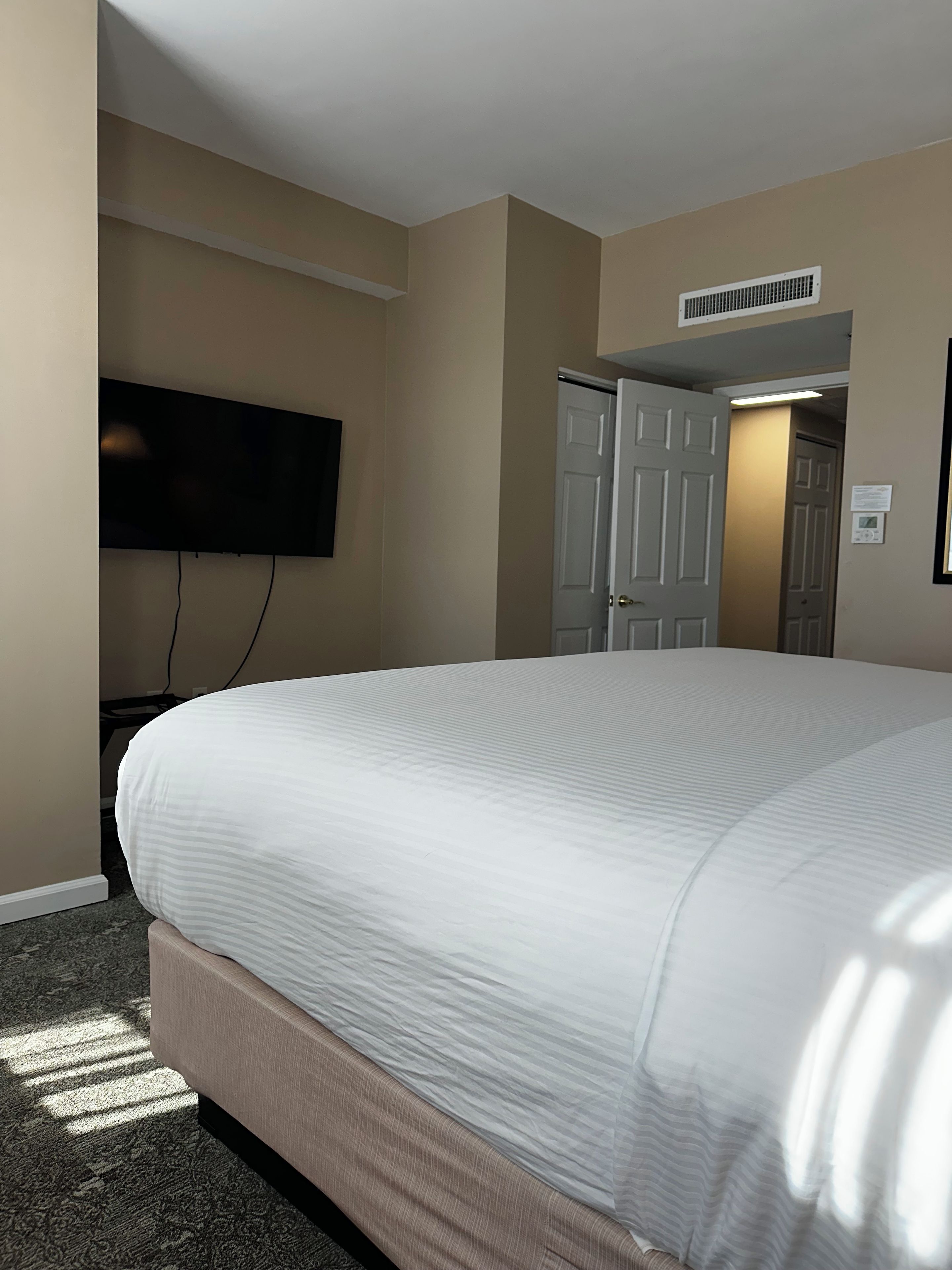 Quarto de hotel com uma cama grande, televisão de tela plana fixada na parede e uma porta que dá para outro quarto.