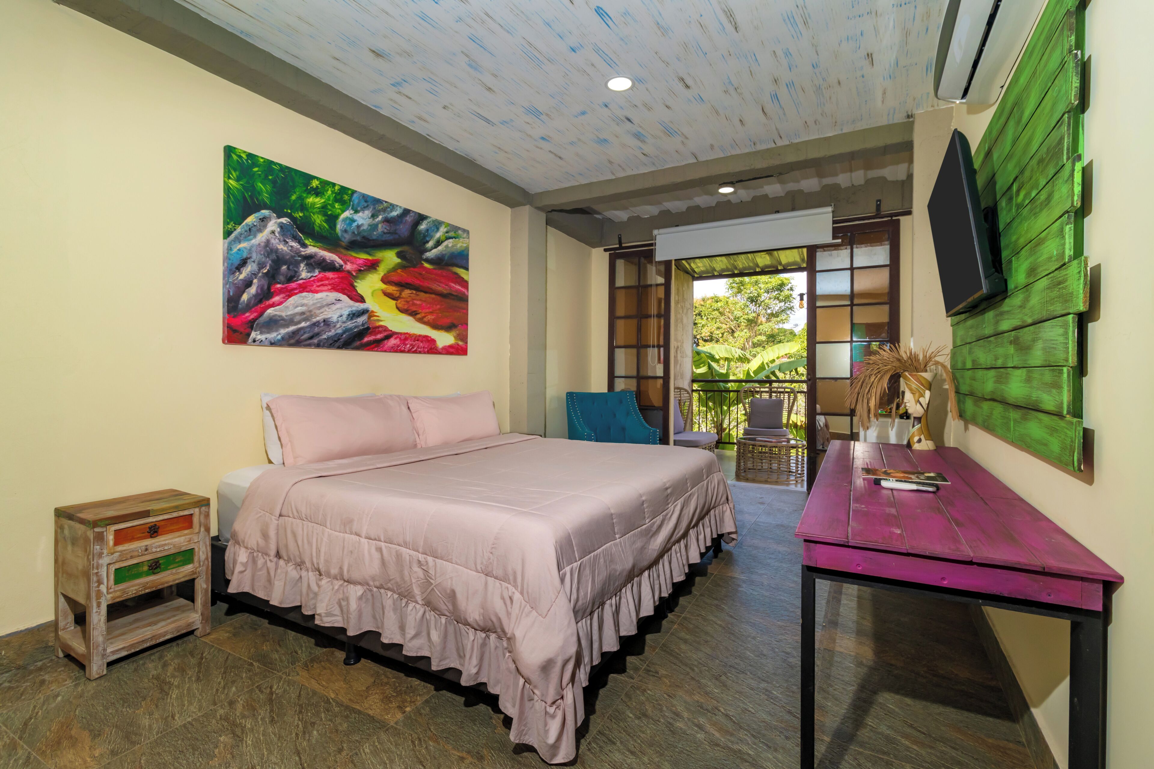 Quarto com cama, pintura, escrivaninha e vista para o exterior.