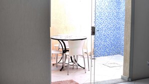 Uma porta de vidro dá acesso a um pátio com parede azul azulejada, uma mesa redonda com cadeiras e um tapete pequeno.