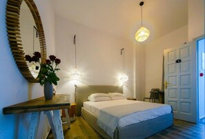 Quarto com cama, mesa de cabeceira, espelho e duas luminárias pendentes.