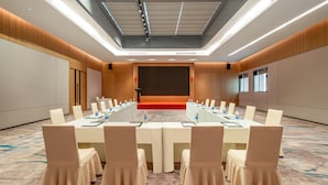 Uma sala de conferências com uma mesa comprida, cadeiras, um pódio e uma tela grande.