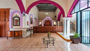 Um hall amplo com tetos altos, portas em arco e uma mesa redonda central.